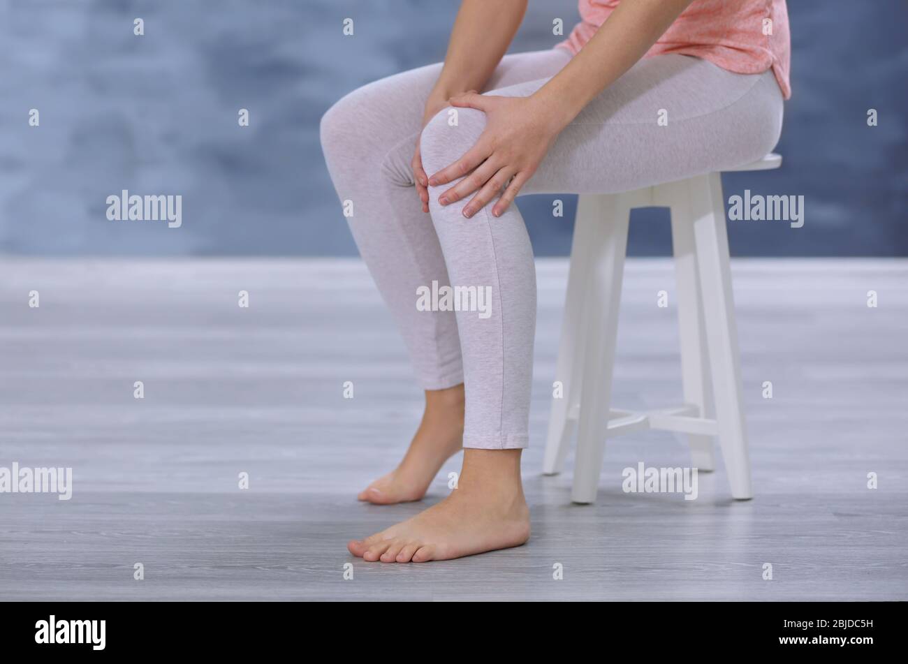 Young woman suffering from knee pain while sitting on stool indoors ...