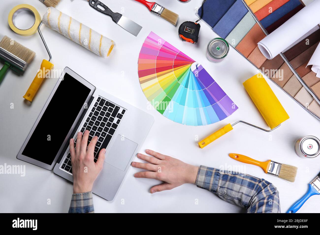 Decorator's hands typing on a laptop. Color swatches with tools on work ...