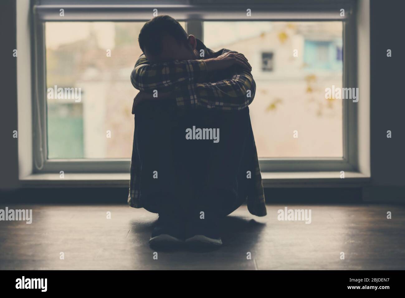 Depressed man sitting on floor near window Stock Photo - Alamy
