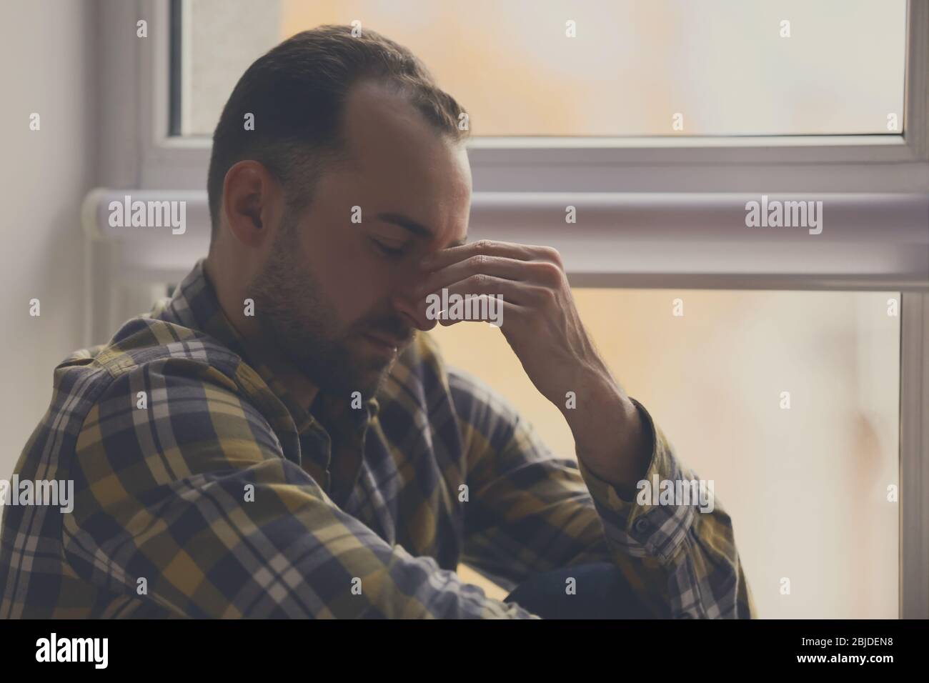 Handsome depressed man sitting near window Stock Photo - Alamy
