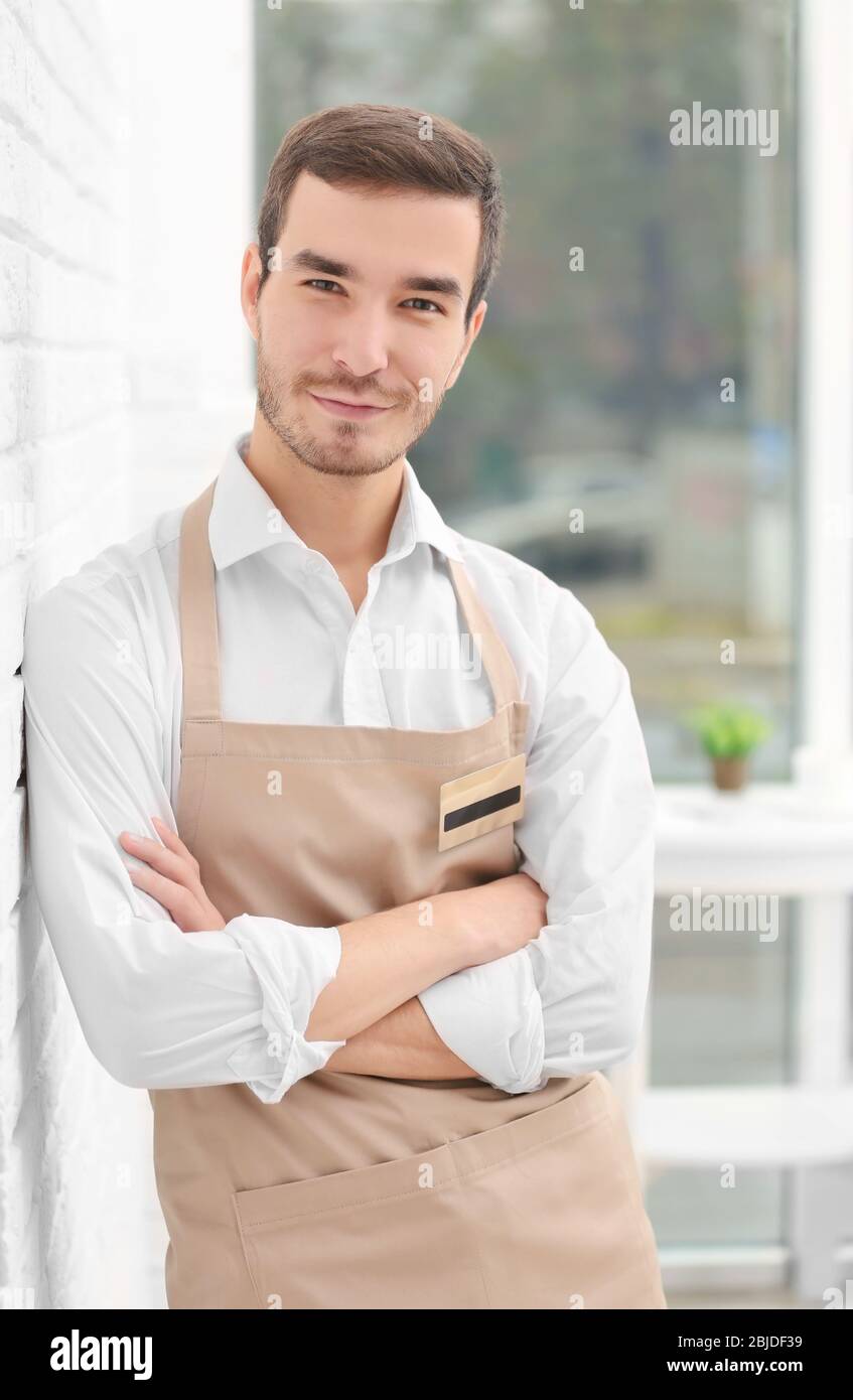 Cute waiter in beige apron on blurred background Stock Photo - Alamy