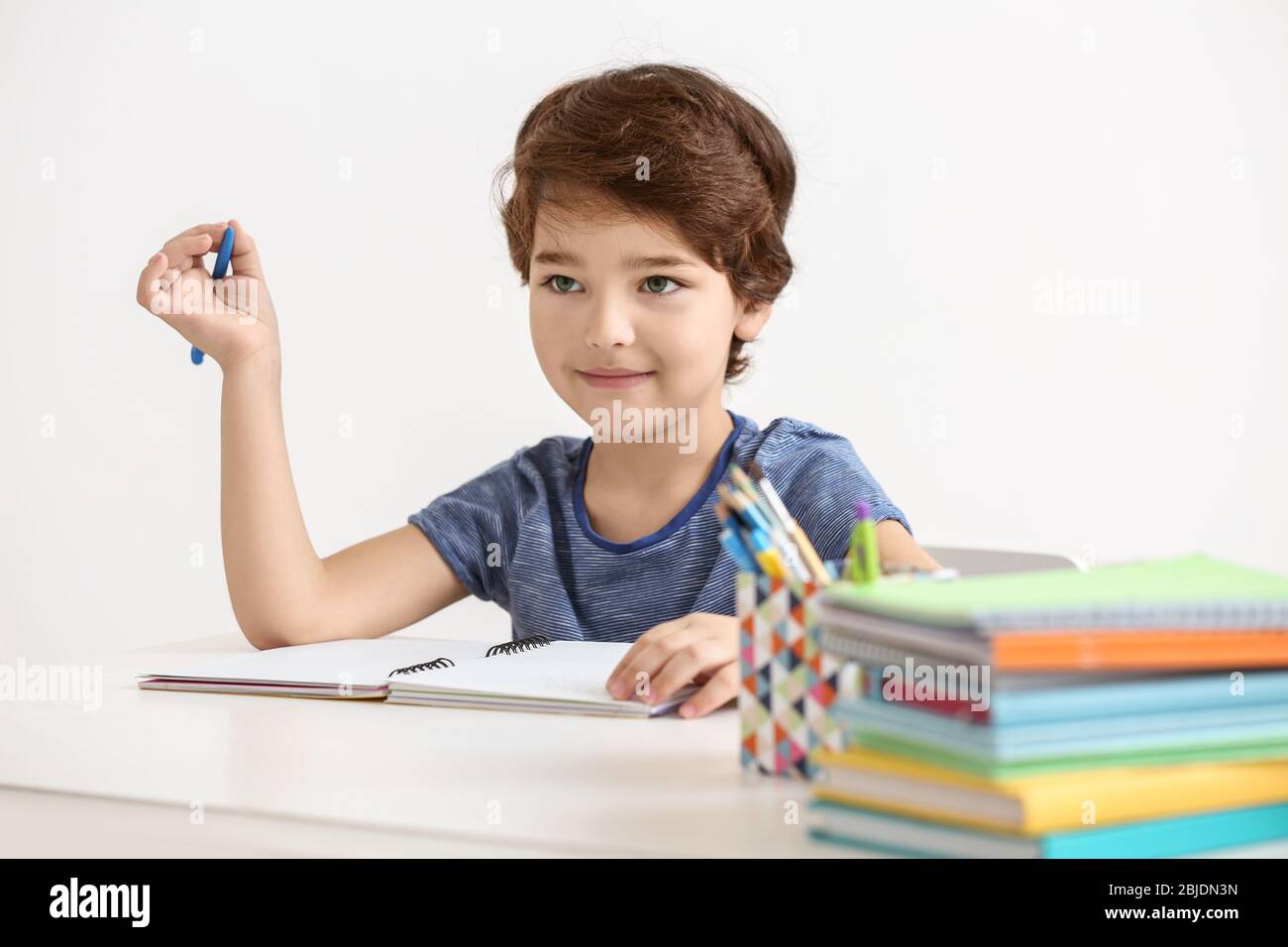 Cute little boy writing something in notebook, on white background ...