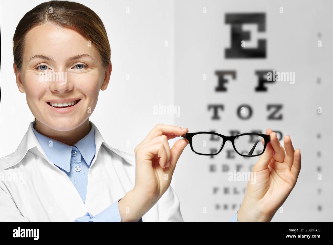 Young woman holding spectacles on eyesight test chart background Stock ...