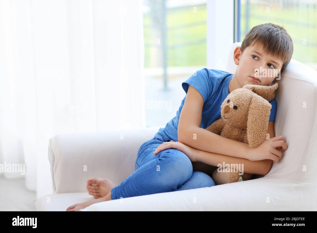 Sad little boy sitting in armchair at home Stock Photo - Alamy