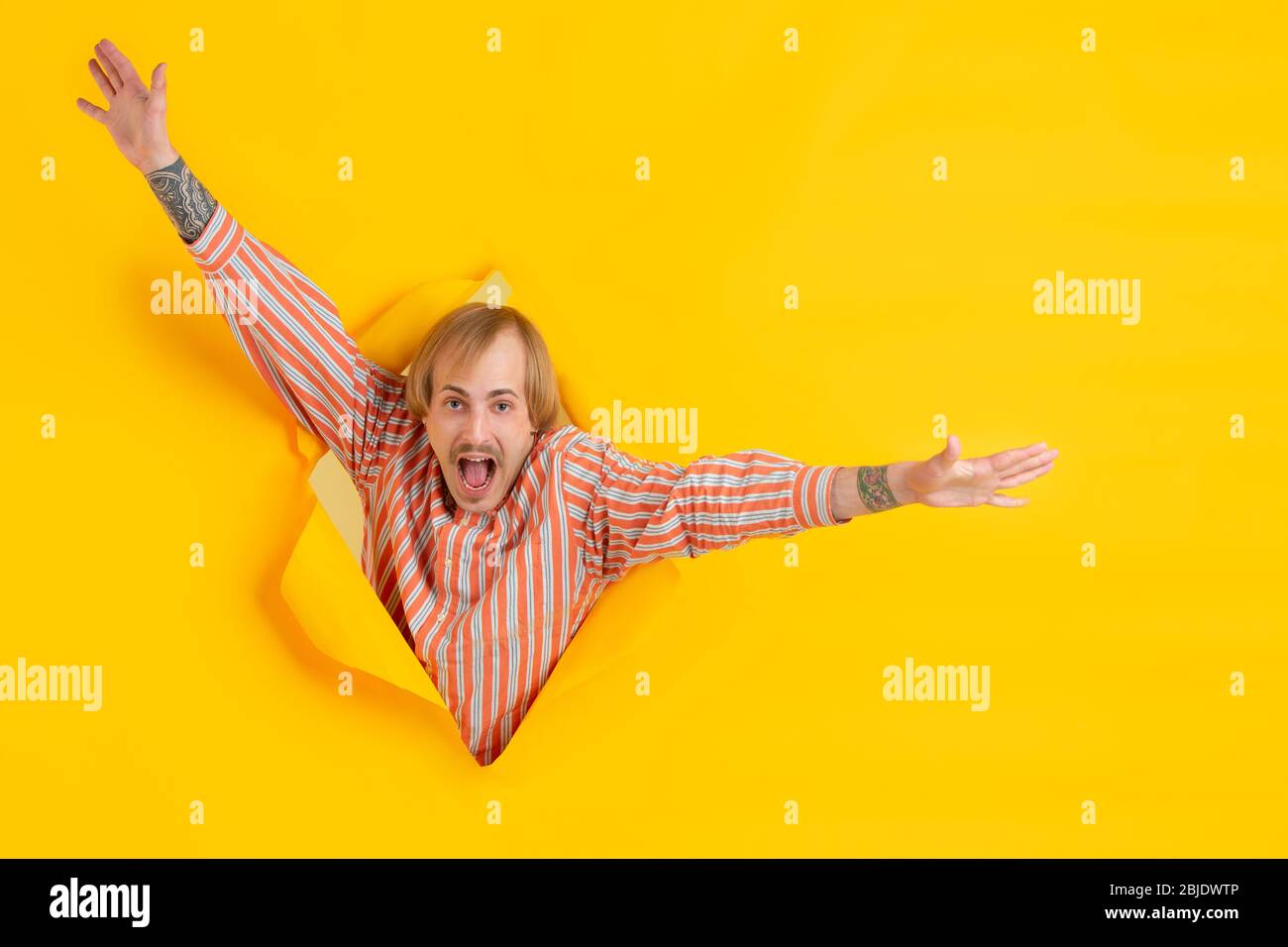 Surprising greeting. Cheerful caucasian young man poses in torn yellow ...