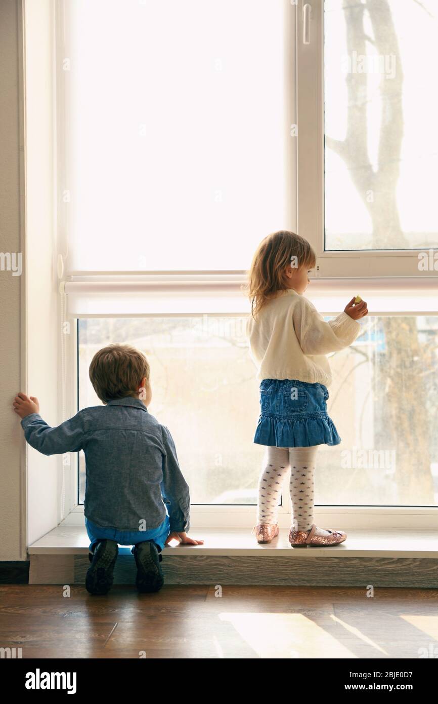 Cute little children near big window at home Stock Photo - Alamy