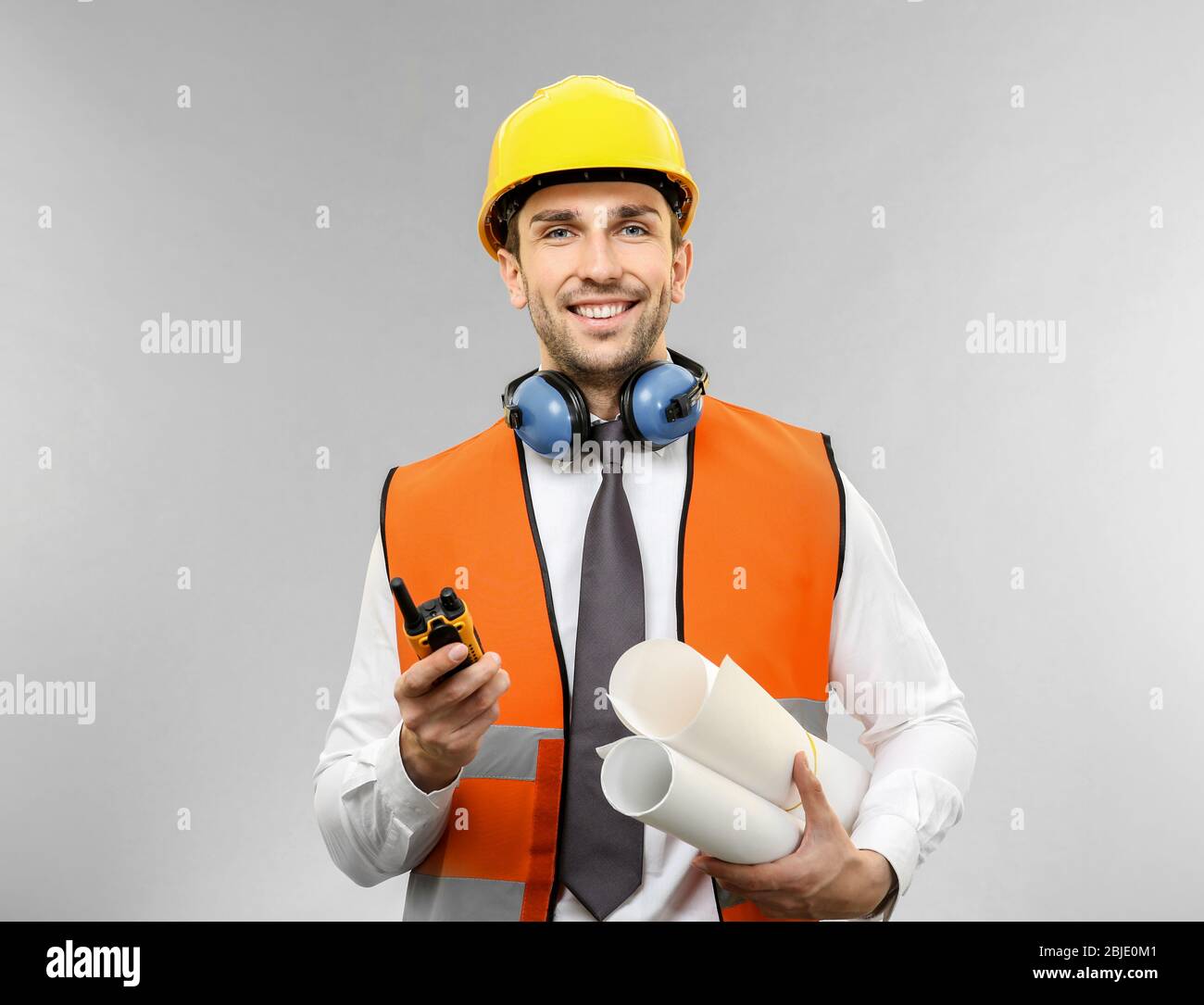 Handsome engineer with portable radio transmitter and drawings on light ...