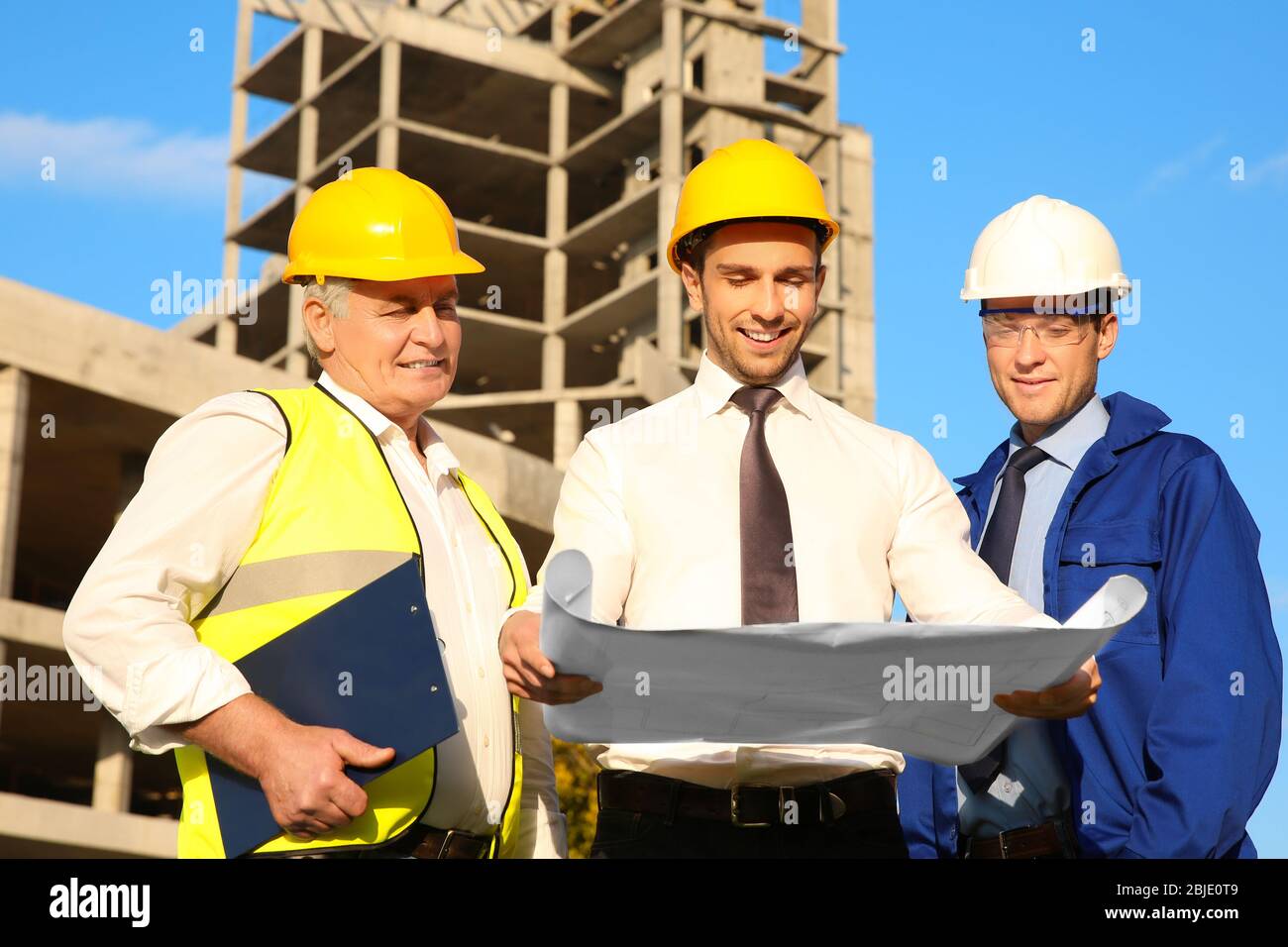 Engineer with drawing and workers standing against unfinished building ...