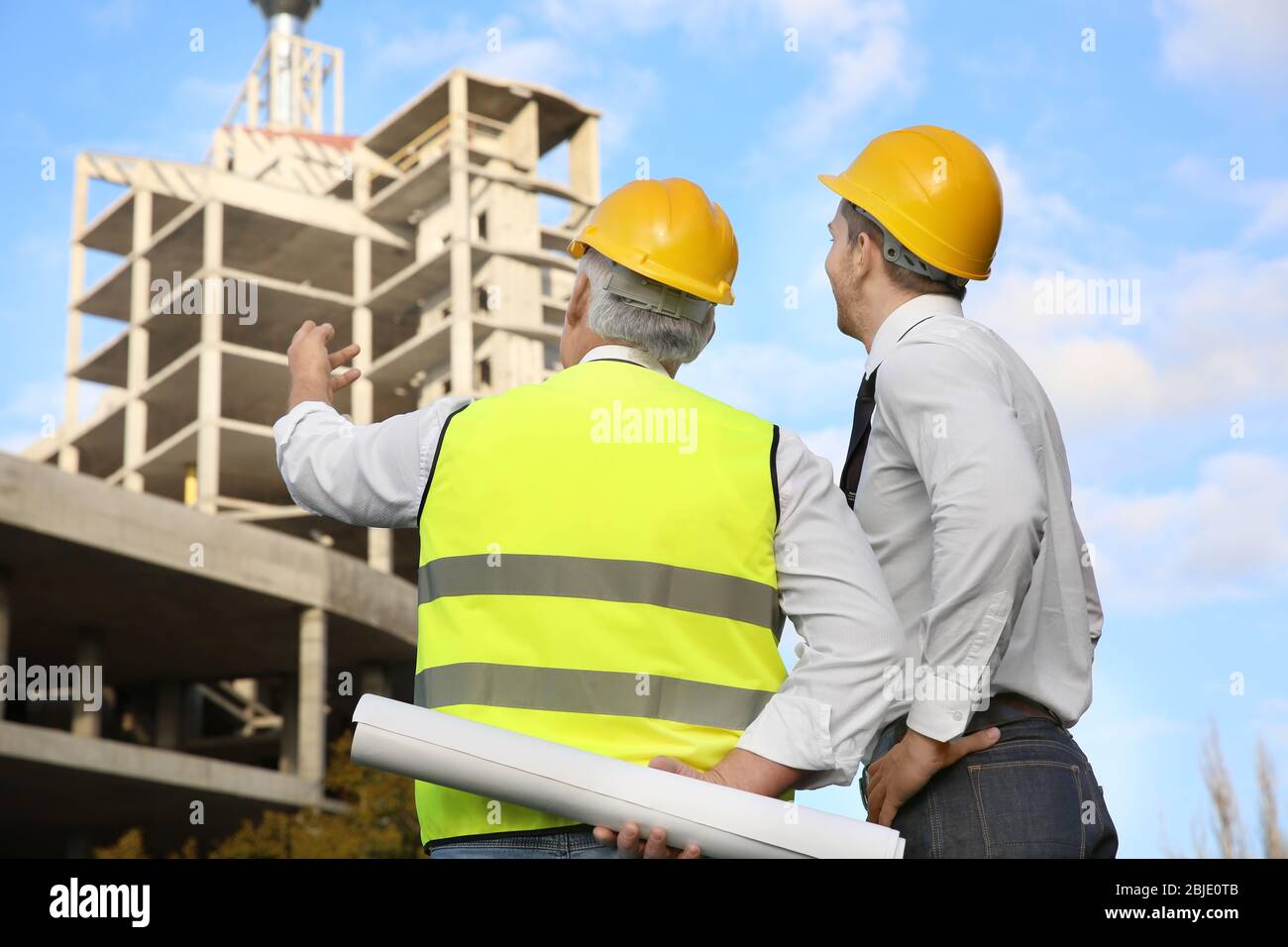 Engineer and worker discussing construction of unfinished building ...