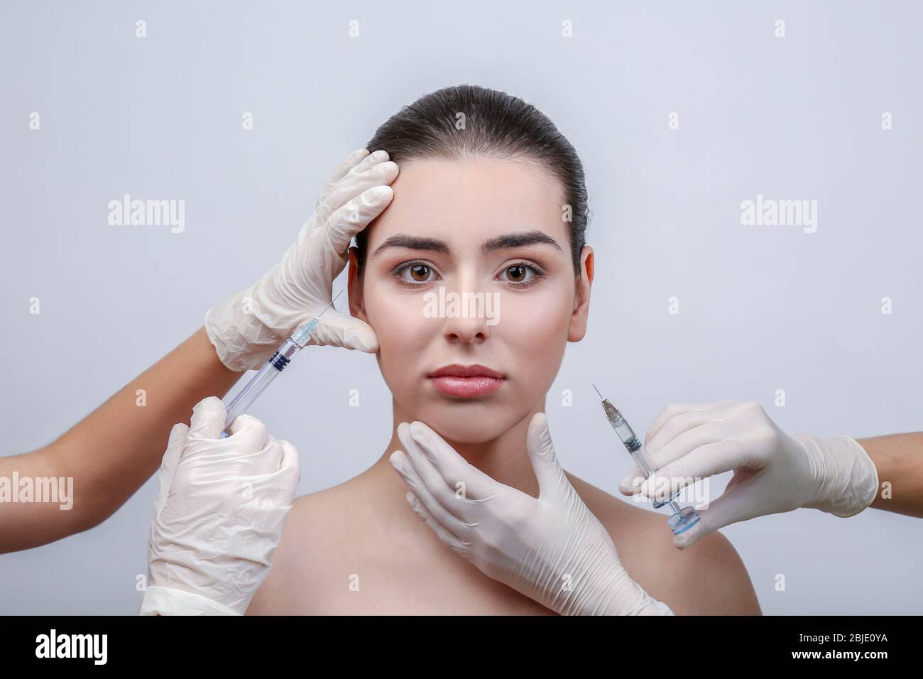 Beautiful young woman receiving filler injections in face, on light ...