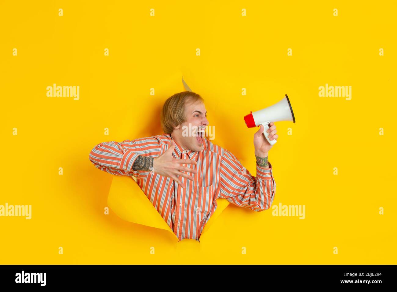 Shouting using speaker. Cheerful caucasian young man poses in torn ...