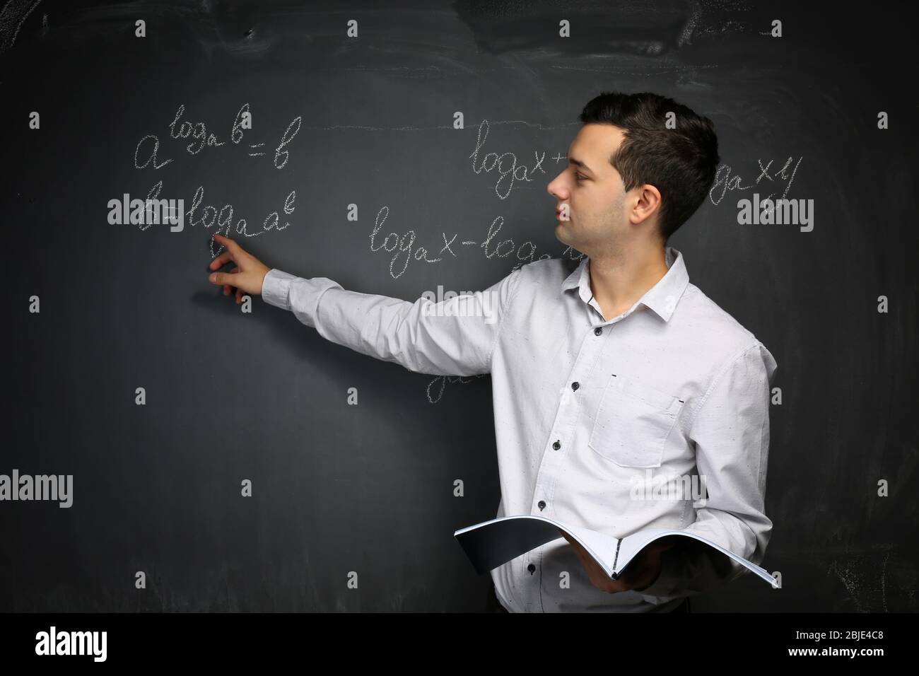 Handsome young teacher explaining math formulas written on blackboard ...