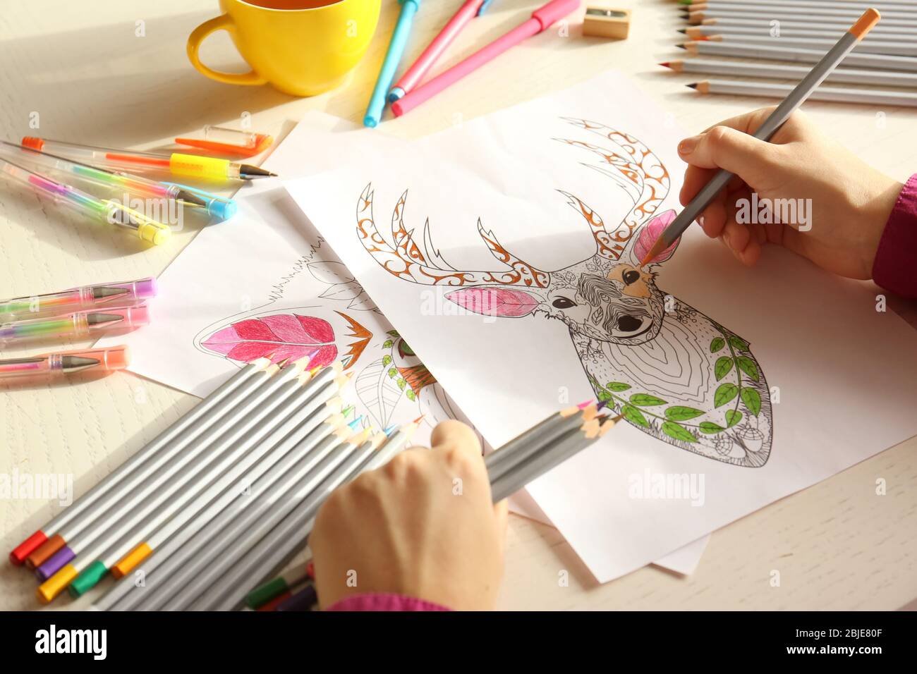 Woman sitting at table with coloring pictures for adults, closeup Stock ...