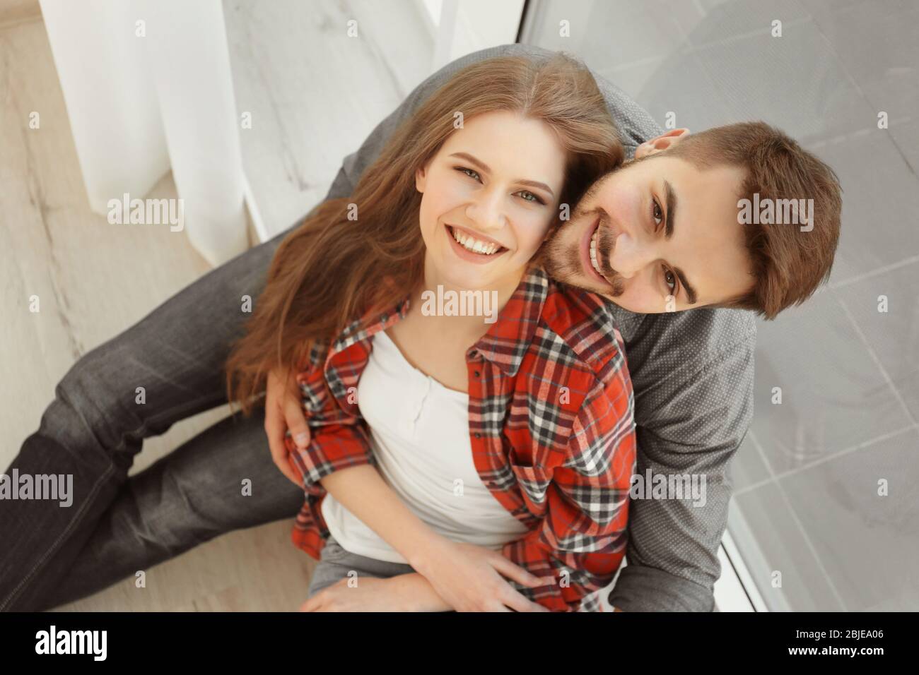 Cute young couple sitting on window sill at home Stock Photo - Alamy