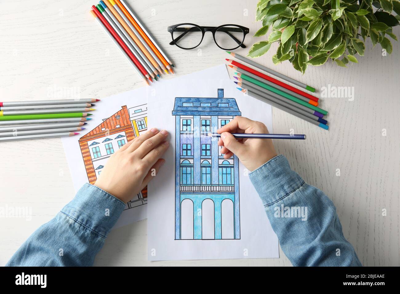 Young woman sitting at table with coloring pictures for adults, closeup ...
