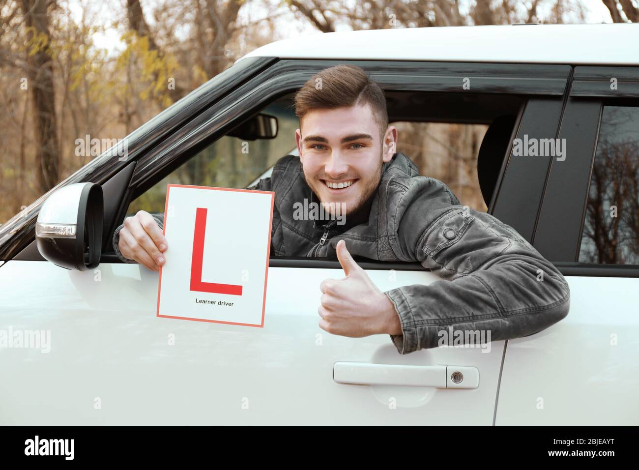 Young man holding learner driver sign while looking out of car window ...