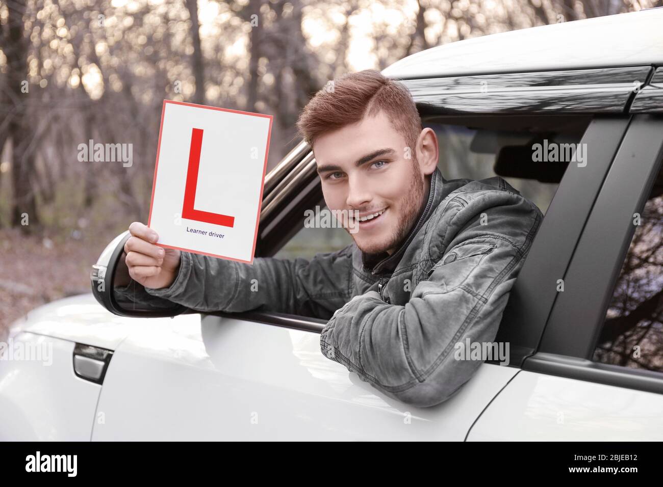 Young man holding learner driver sign while looking out of car window ...