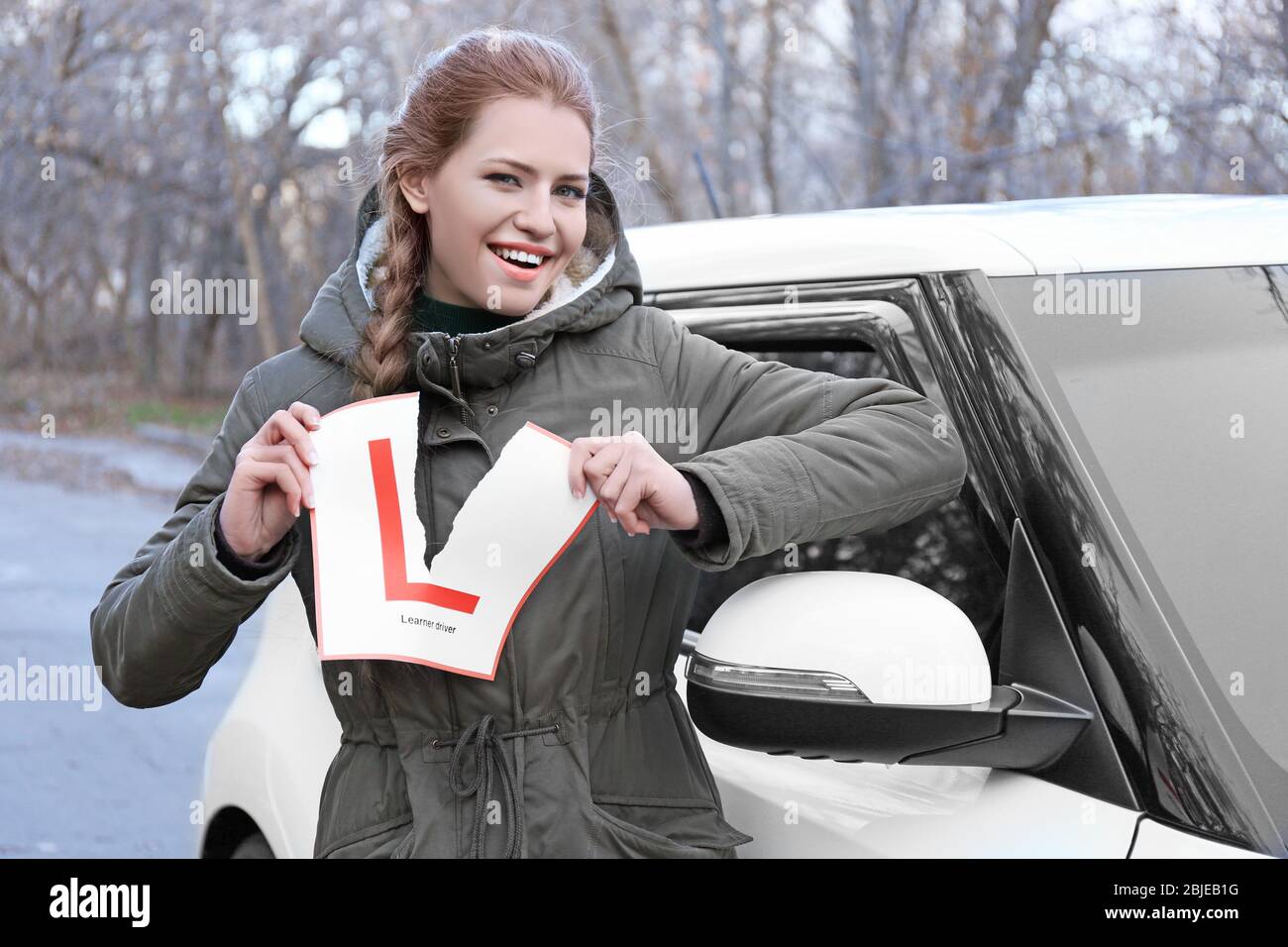 Happy young woman tearing learner driver sign while standing near car ...