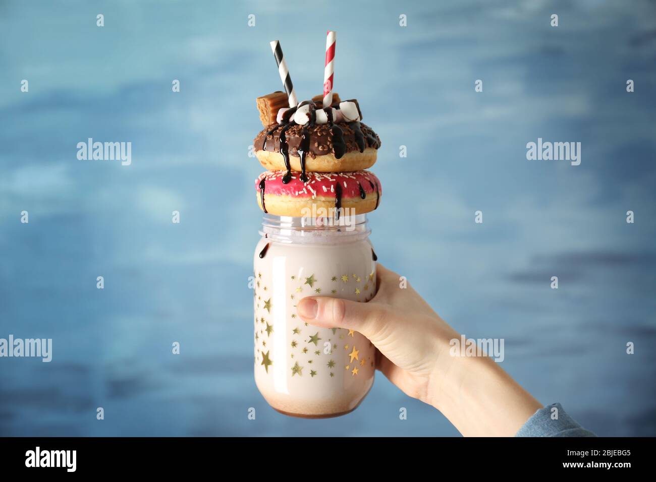Hand holding milkshake, donuts and other sweets in jar on blue ...