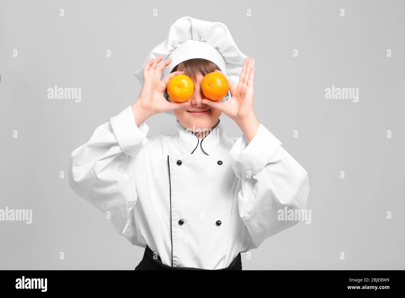 Cute boy in chef uniform on light background Stock Photo - Alamy