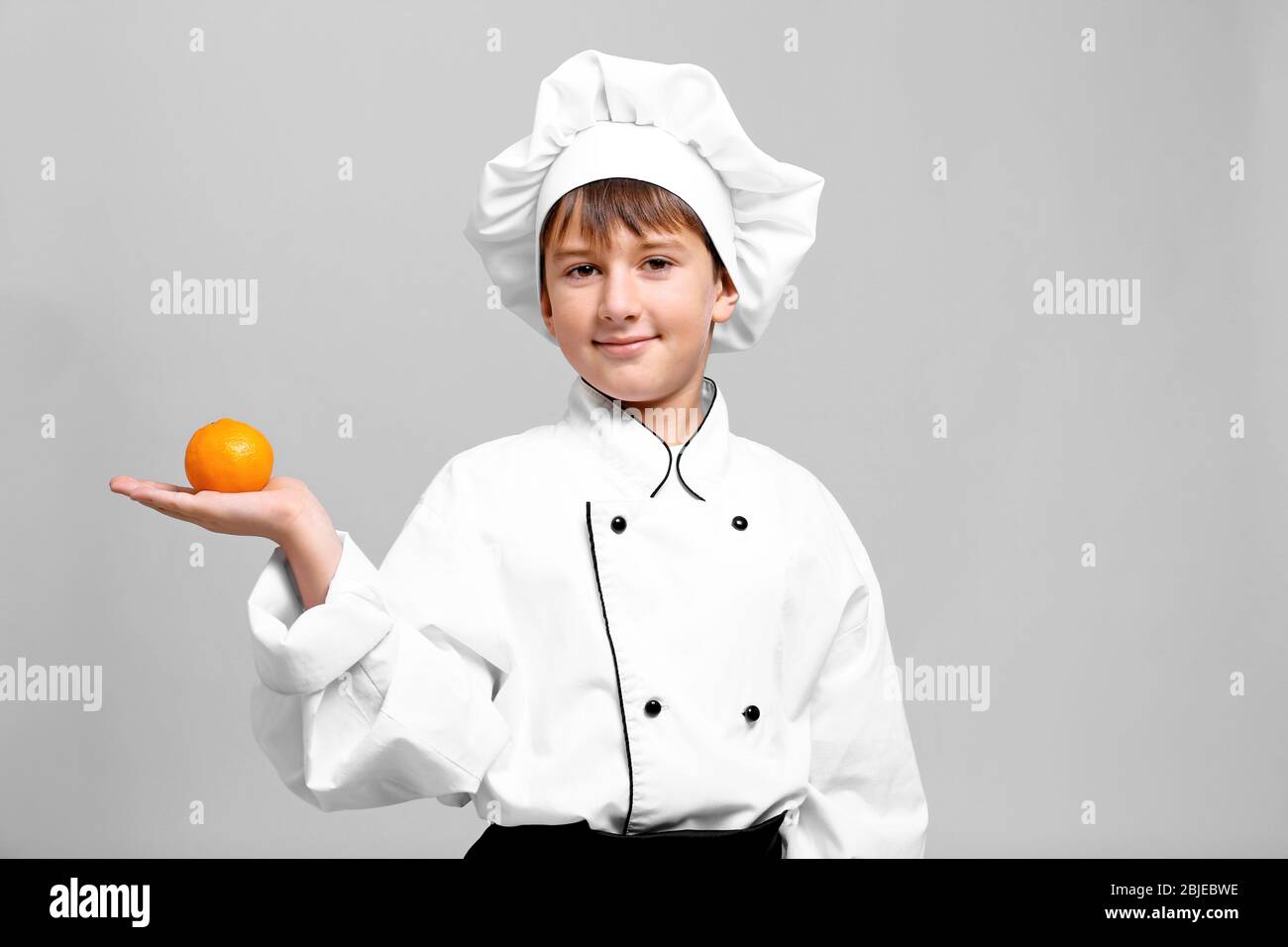 Cute boy in chef uniform on light background Stock Photo - Alamy