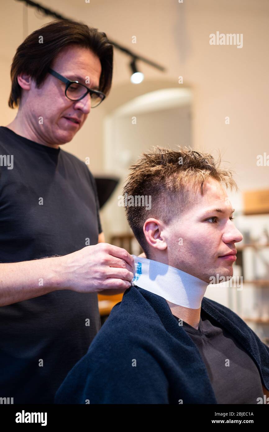 Barber attaches ruff to the neck of a young man in his barbershop ...