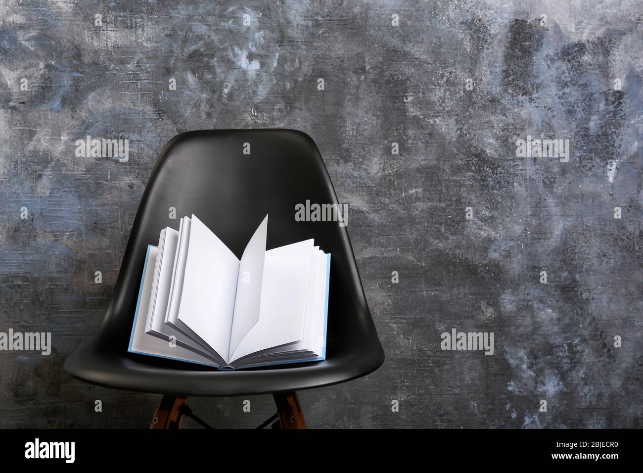 Open book on chair against gray wall background Stock Photo - Alamy