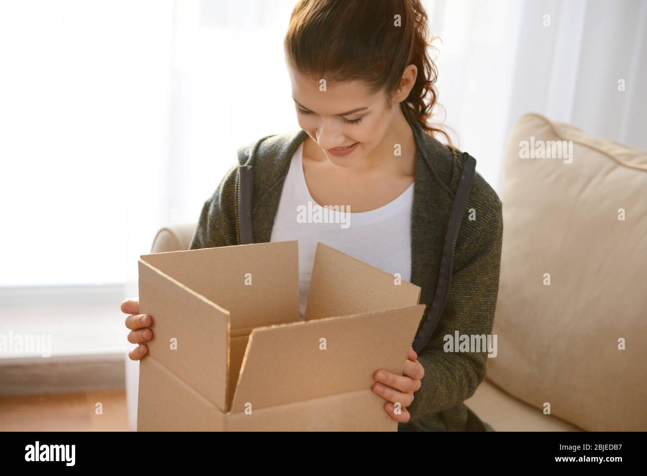 Beautiful young woman opening box with parcel at home Stock Photo - Alamy