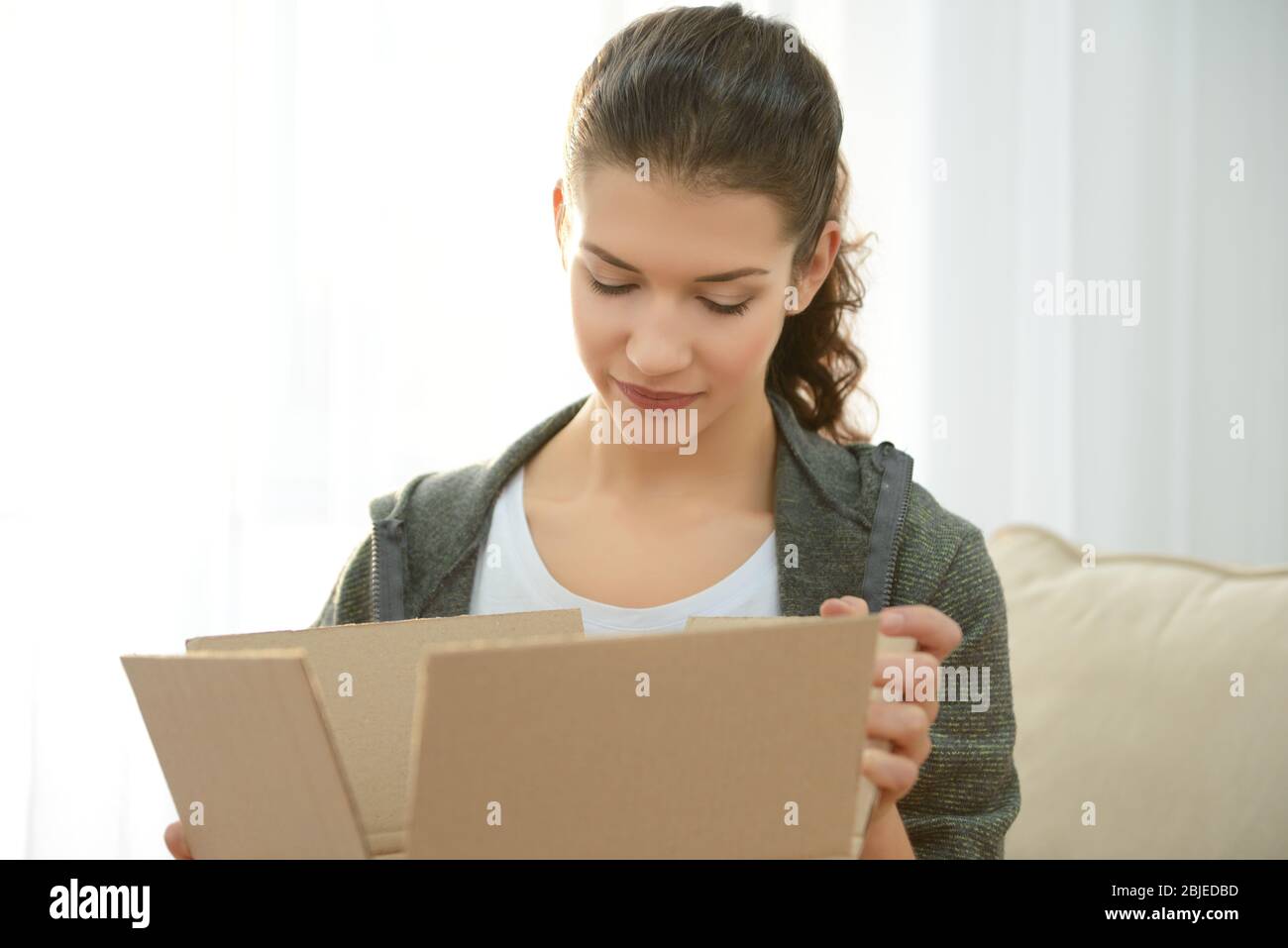 Beautiful young woman opening box with parcel at home Stock Photo - Alamy