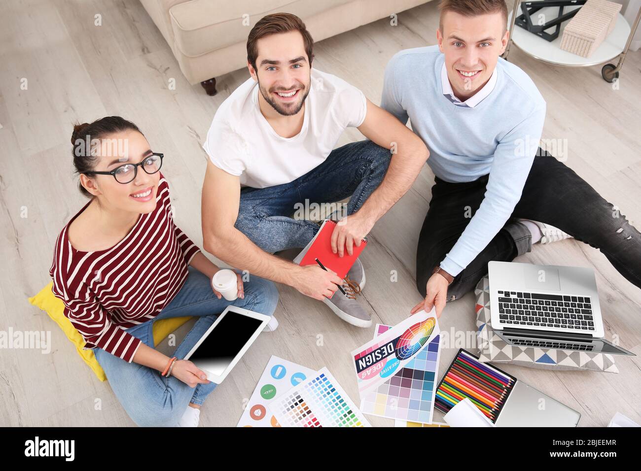 Three young designers sitting on floor of office room Stock Photo - Alamy
