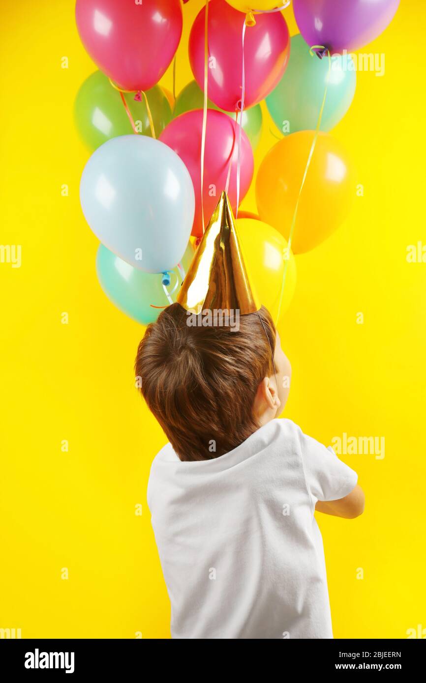 Cute birthday boy with colorful balloons on yellow background Stock ...