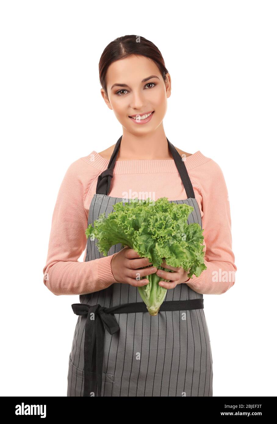 Young woman in apron holding bunch of fresh lettuce on white background ...