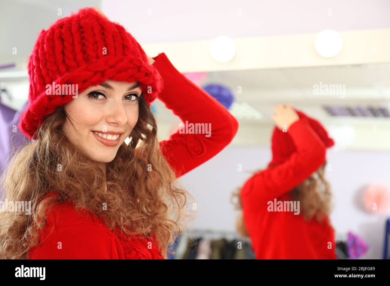 Beautiful young woman trying on knitted cap in modern shop Stock Photo ...
