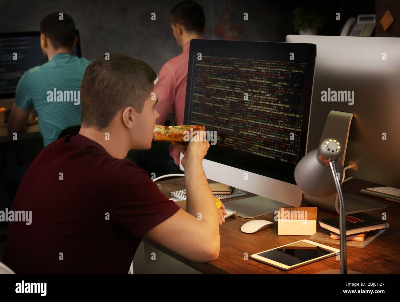 Young programmer eating pizza while working in office Stock Photo - Alamy