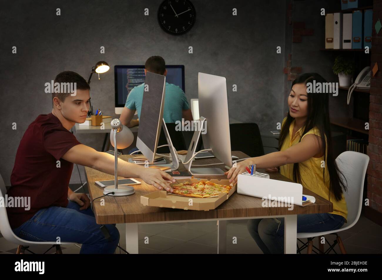 Young programmers eating pizza while working in office Stock Photo - Alamy