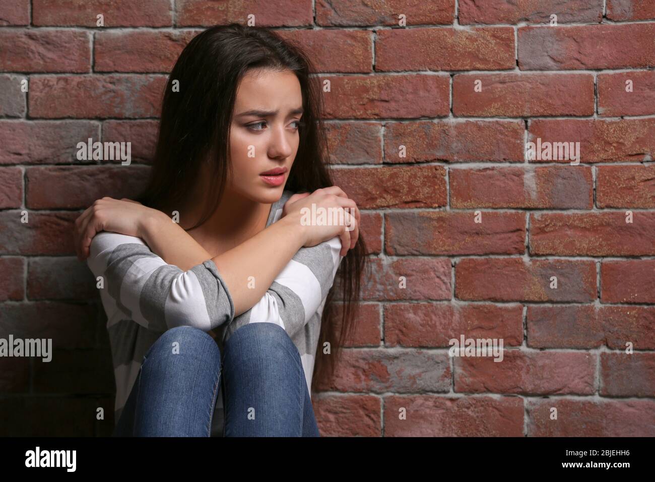 Depressed young woman on brick wall background Stock Photo - Alamy