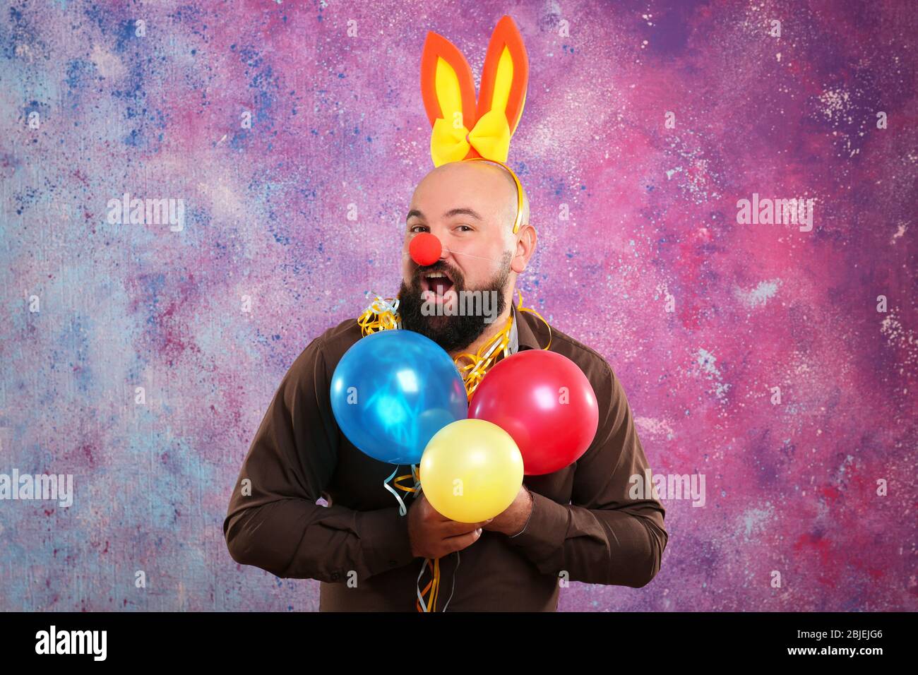 Funny fat man with party decor, balloons and bunny ears on color ...