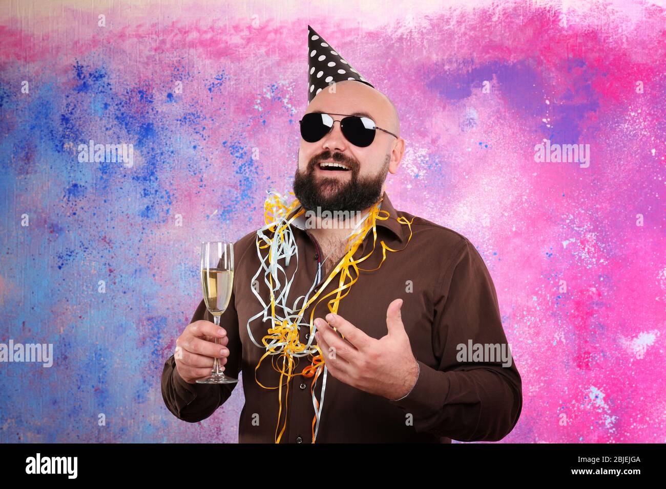 Funny fat man with party hat and glass of champagne on color background ...