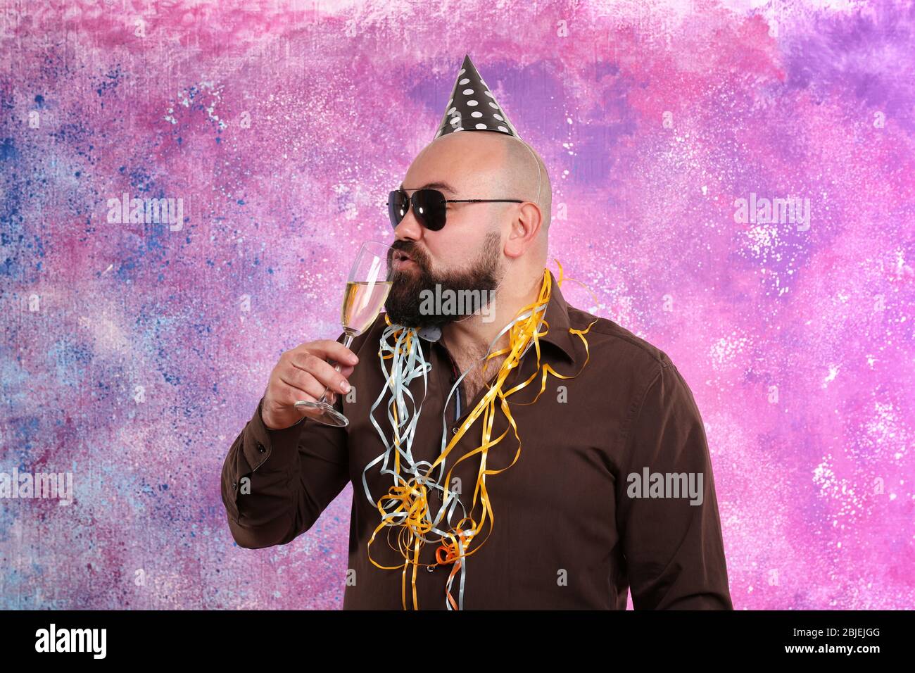Funny fat man with party hat drinking champagne, on color background ...