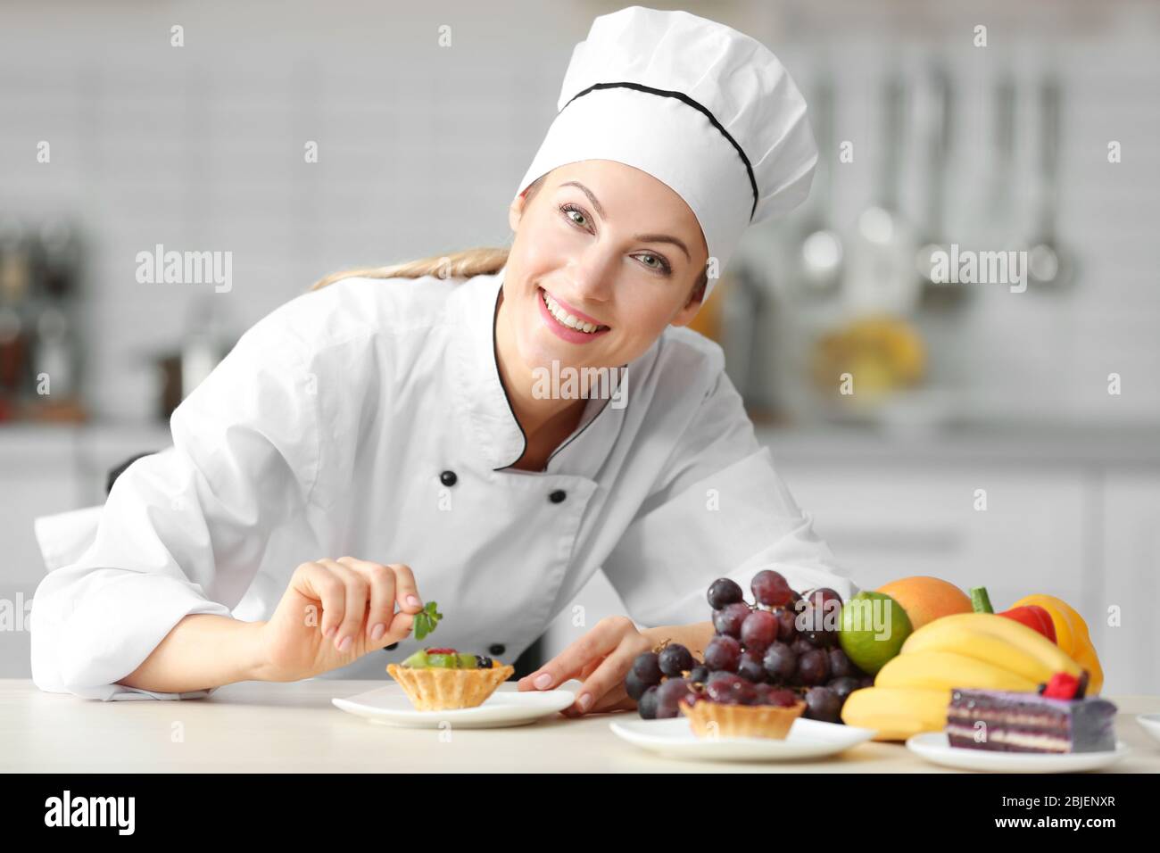 Female chef decorating fruit tartlet in kitchen Stock Photo - Alamy