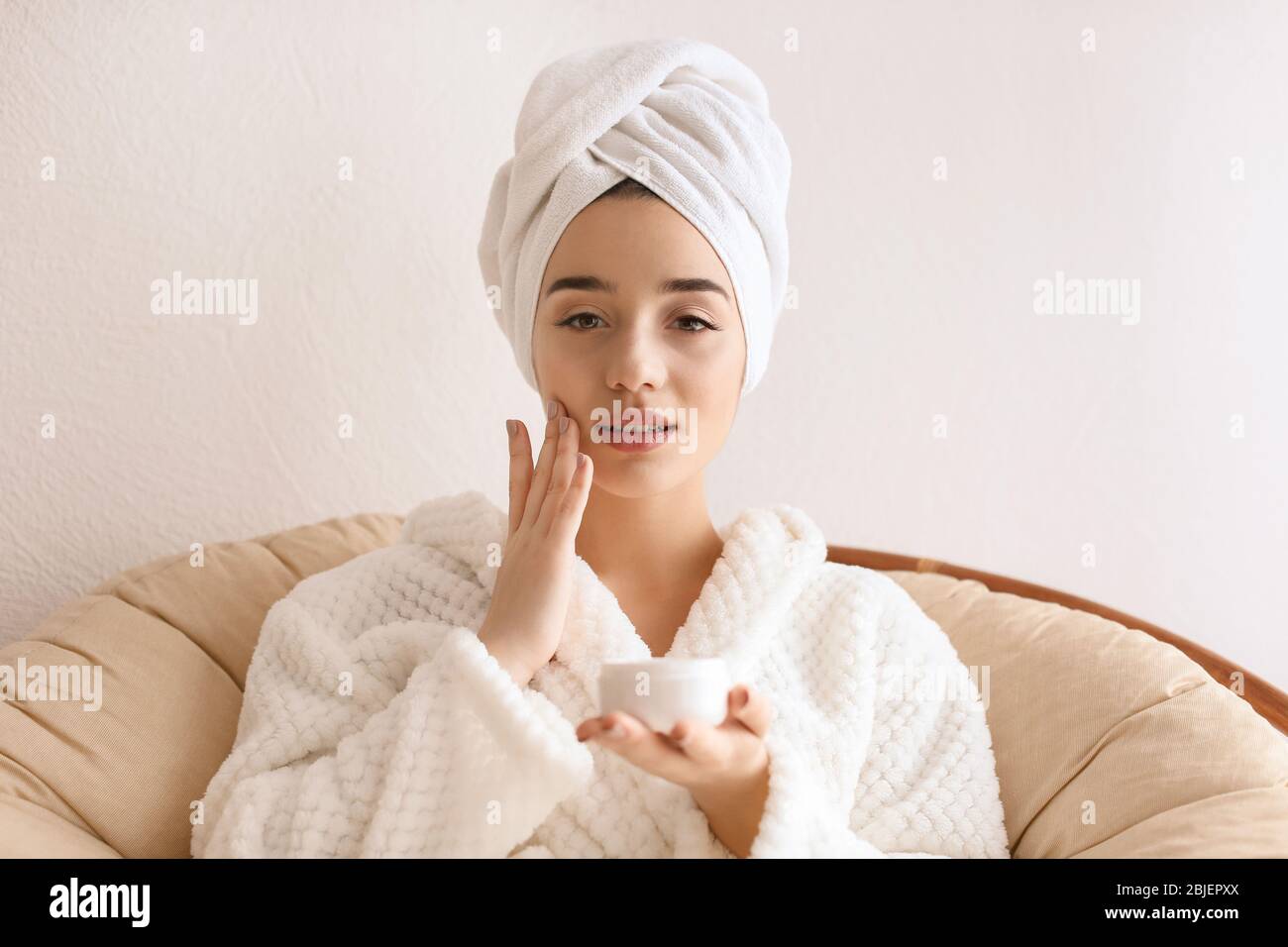 Beautiful young woman applying cream onto skin in spa salon Stock Photo ...