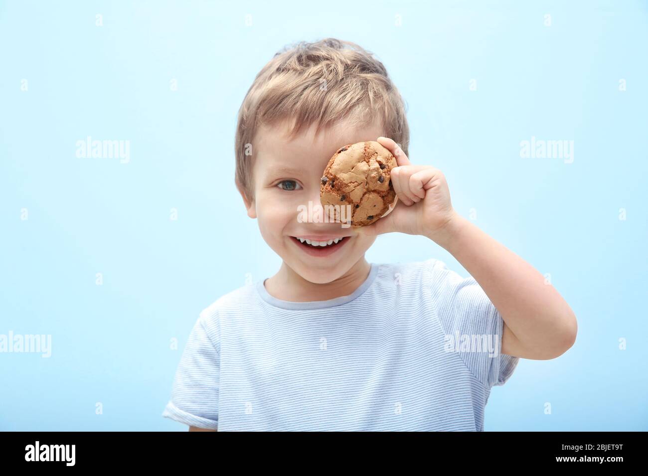 Cute little boy holding cookie on light background Stock Photo - Alamy