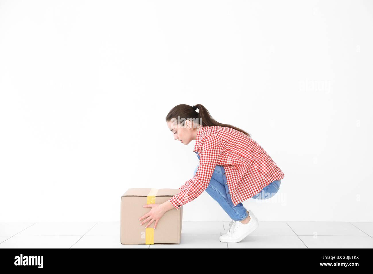 Posture concept. Young woman lifting heavy cardboard box against white ...