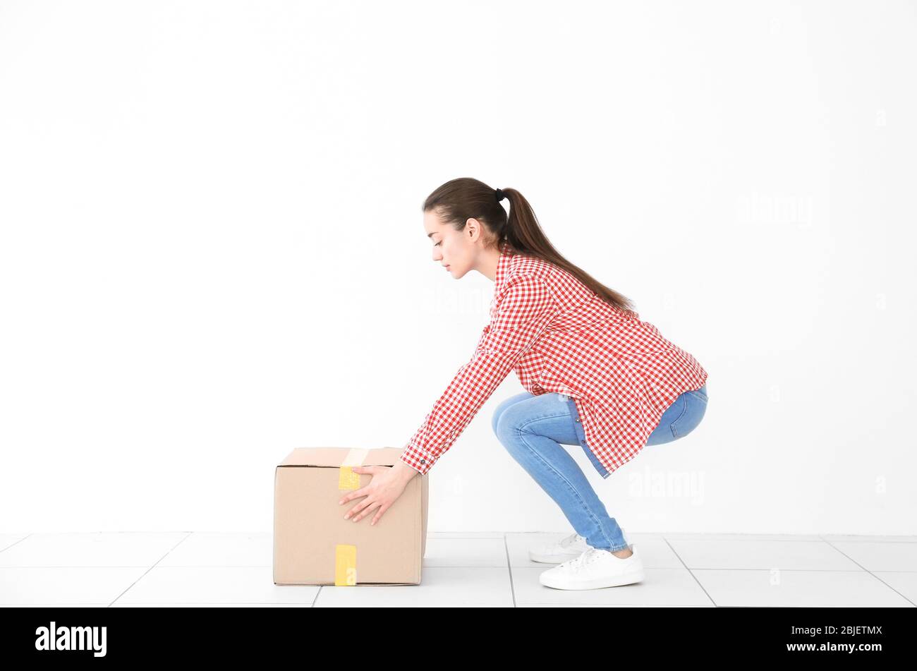 Posture concept. Young woman lifting heavy cardboard box against white ...