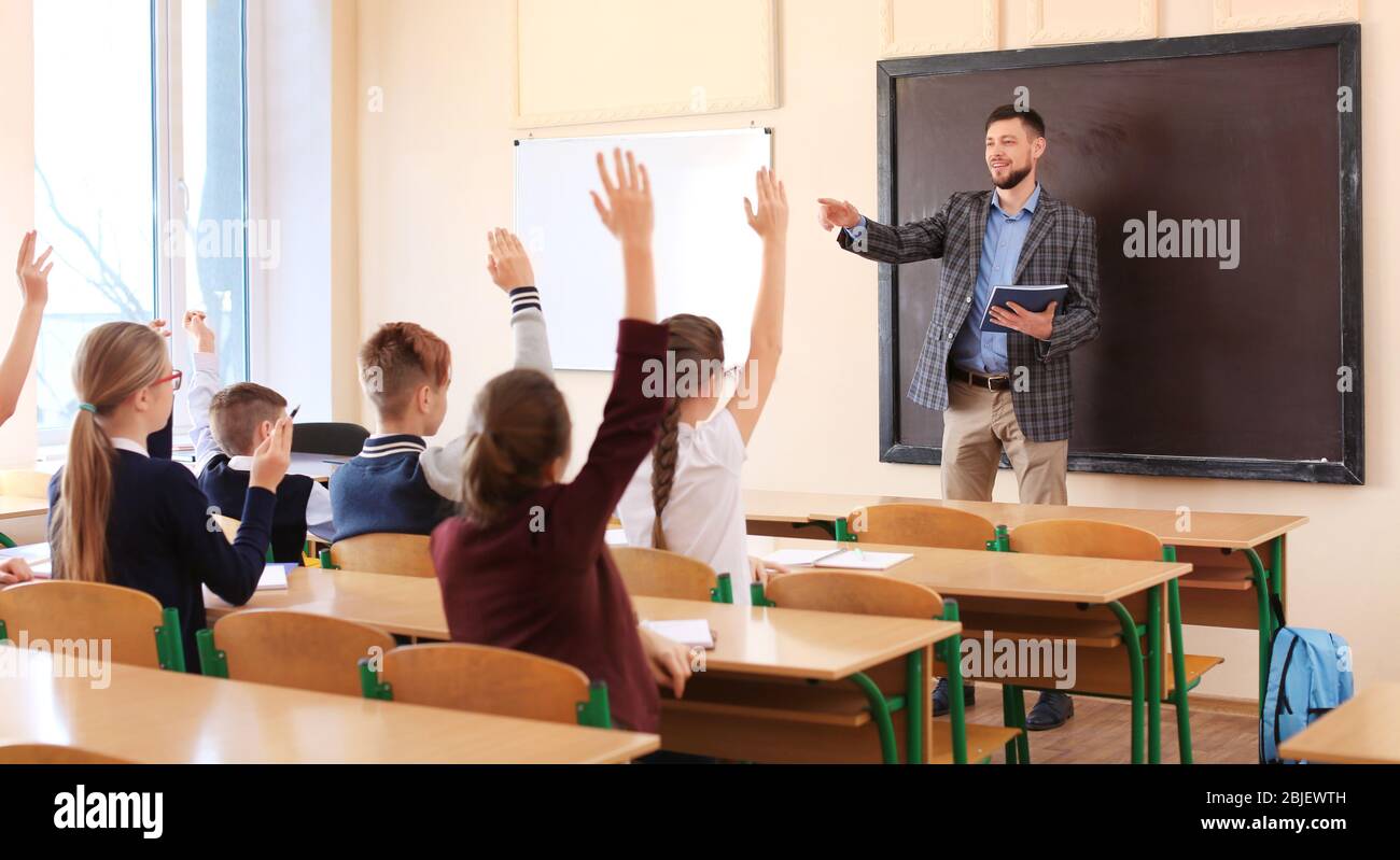 Pupils listening teacher and raising hands to answer in classroom Stock ...