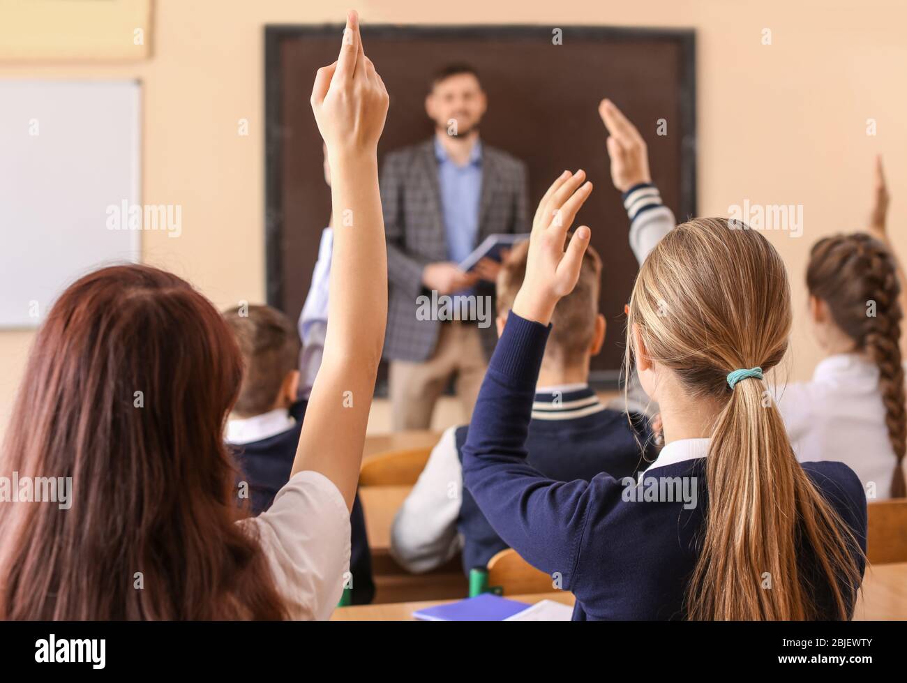 Pupils listening teacher and raising hands to answer in classroom Stock ...