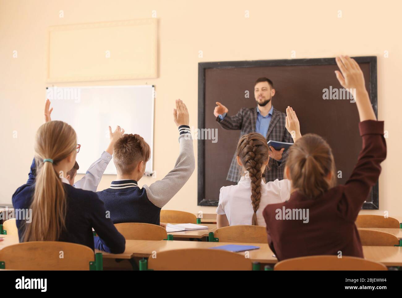Pupils listening teacher and raising hands to answer in classroom Stock ...