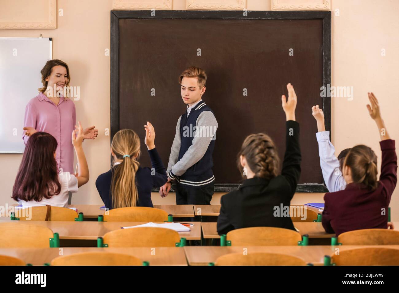 Pupils listening teacher and raising hands to answer in classroom Stock ...