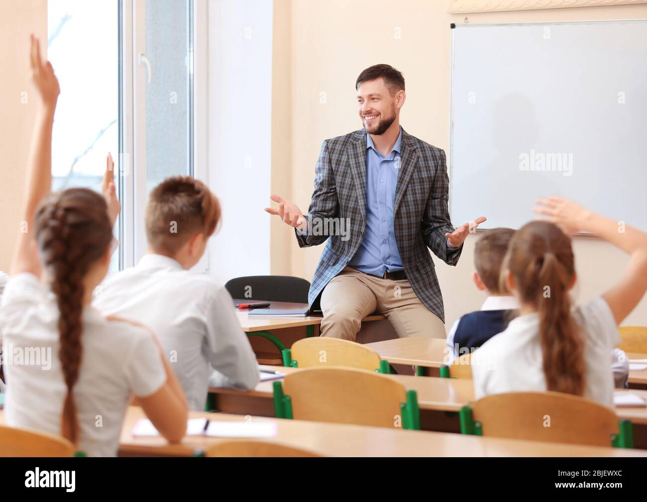 Pupils listening teacher and raising hands to answer in classroom Stock ...