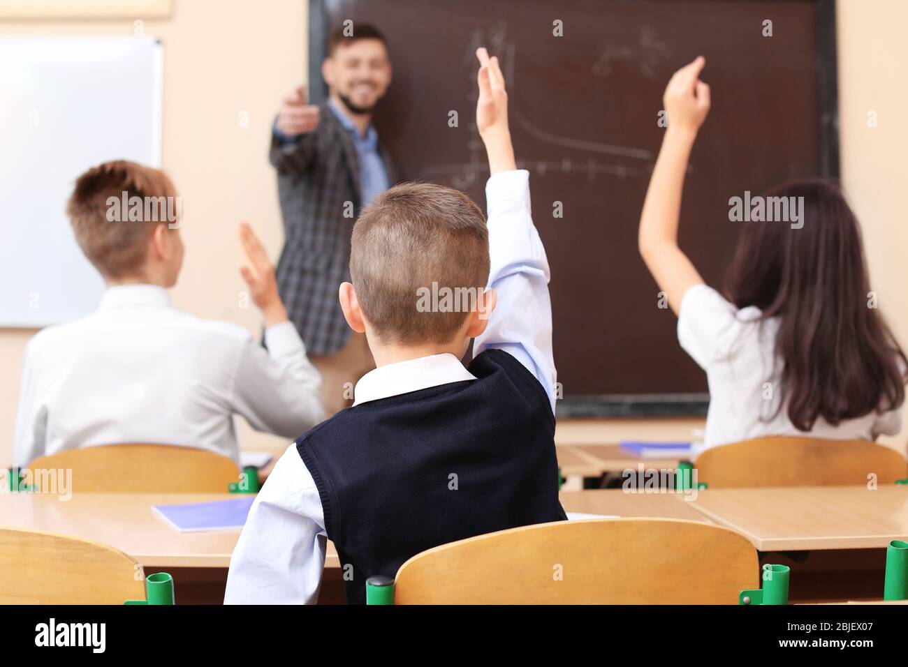 Pupils listening teacher and raising hands to answer in classroom Stock ...